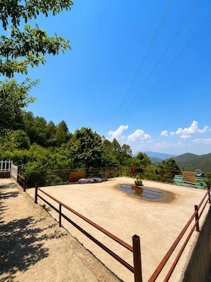Um espaço ao ar livre cercado por árvores e vista para uma montanha, com piso de concreto.