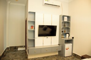 Uma sala de estar moderna com TV de tela plana fixada na parede, um móvel embutido com prateleiras e uma pequena geladeira.