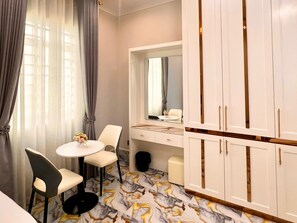 Quarto de hotel com uma cama, uma mesa redonda com duas cadeiras, uma toucador com espelho e um guarda-roupa com duas portas.