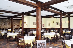 Um restaurante com várias mesas e cadeiras, vigas de madeira no teto e paredes de pedra.