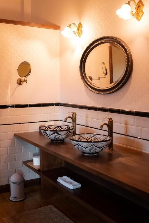 Uma casa de banho com duas pias sobrepostas, um espelho redondo e luminárias de parede.