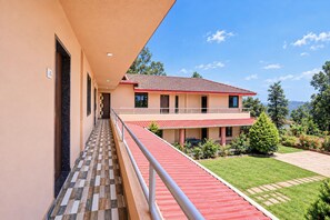 Um hotel com telhado de telhas vermelhas, varanda com guarda-corpo de metal e vista para a vegetação e colinas ao redor.
