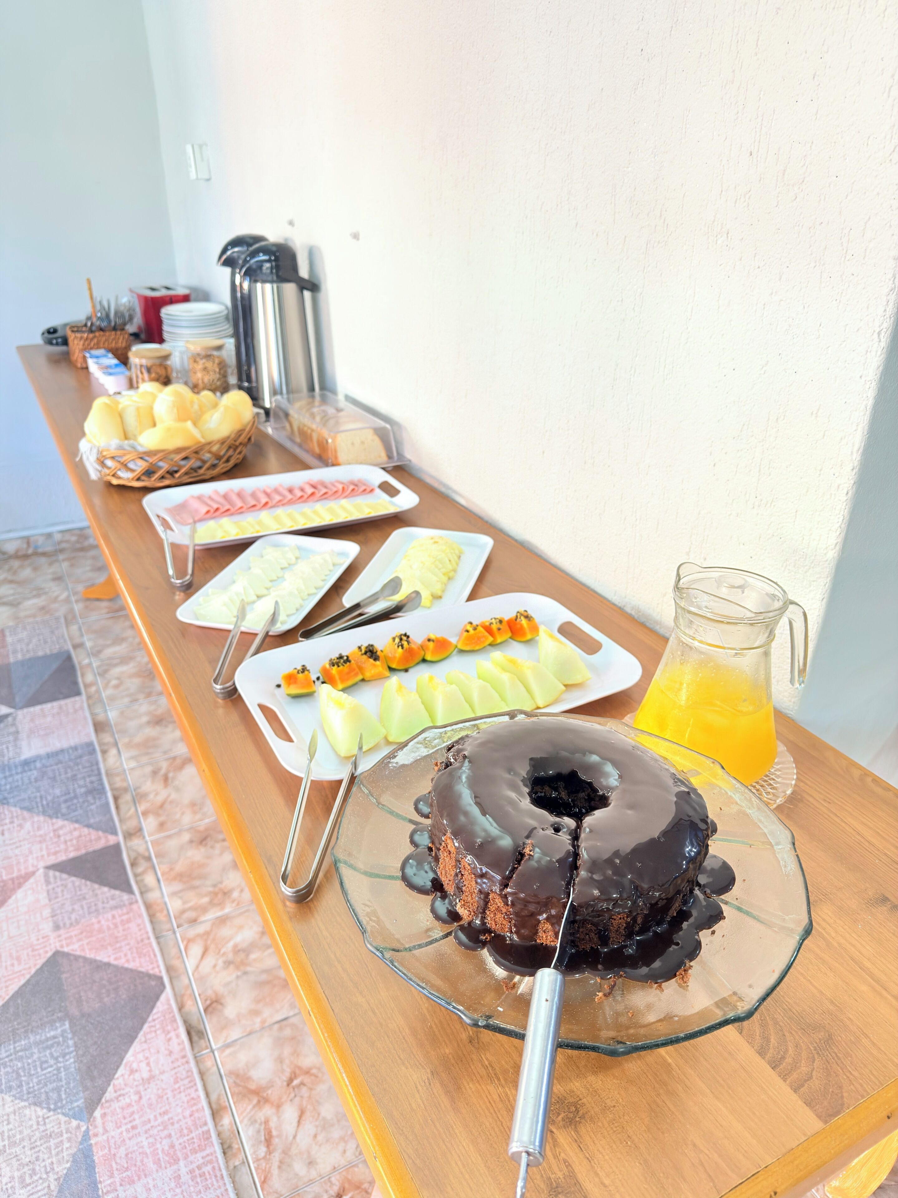 Mesa de buffet com diversos alimentos e um jarro de suco de laranja.