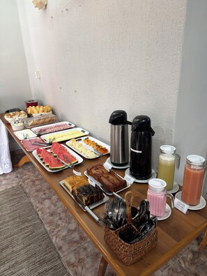 Mesa de buffet com diversos alimentos, máquinas de café e um dispensador de bebidas.