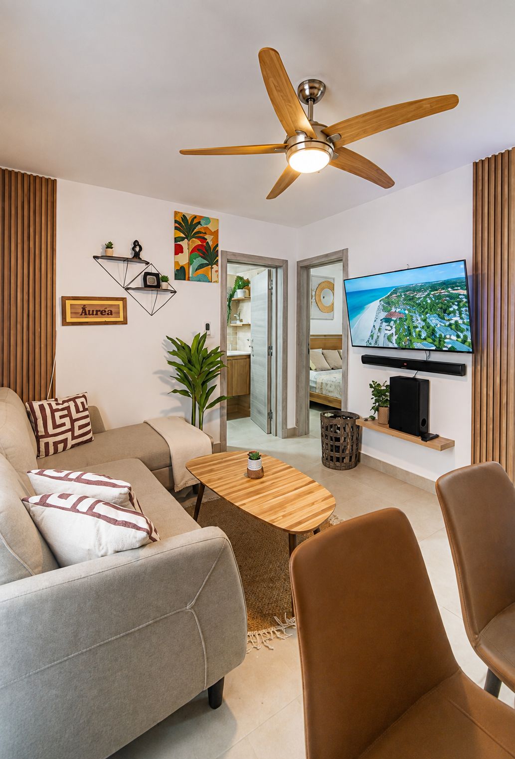 Uma sala de estar moderna com sofá, mesa de centro, cadeiras, ventoinha no teto, televisão e uma planta.