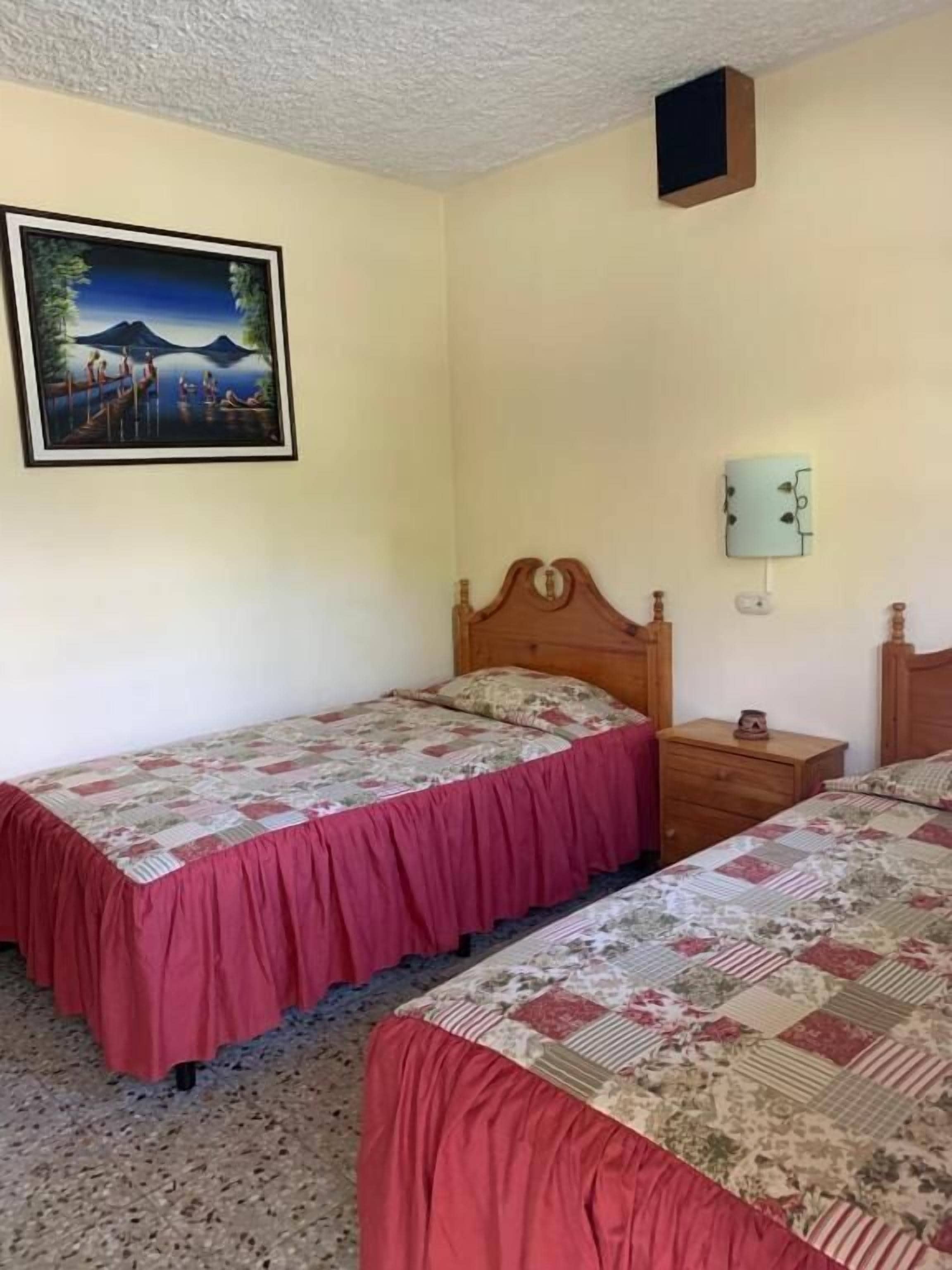 Quarto com duas camas, uma mesa de cabeceira, uma luminária na parede e um quadro emoldurado.