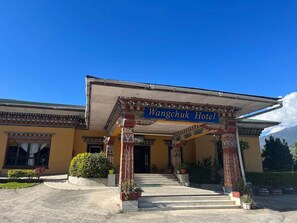 Um edifício com uma placa indicando 'Wangchuk Hotel' e uma entrada coberta com degraus.