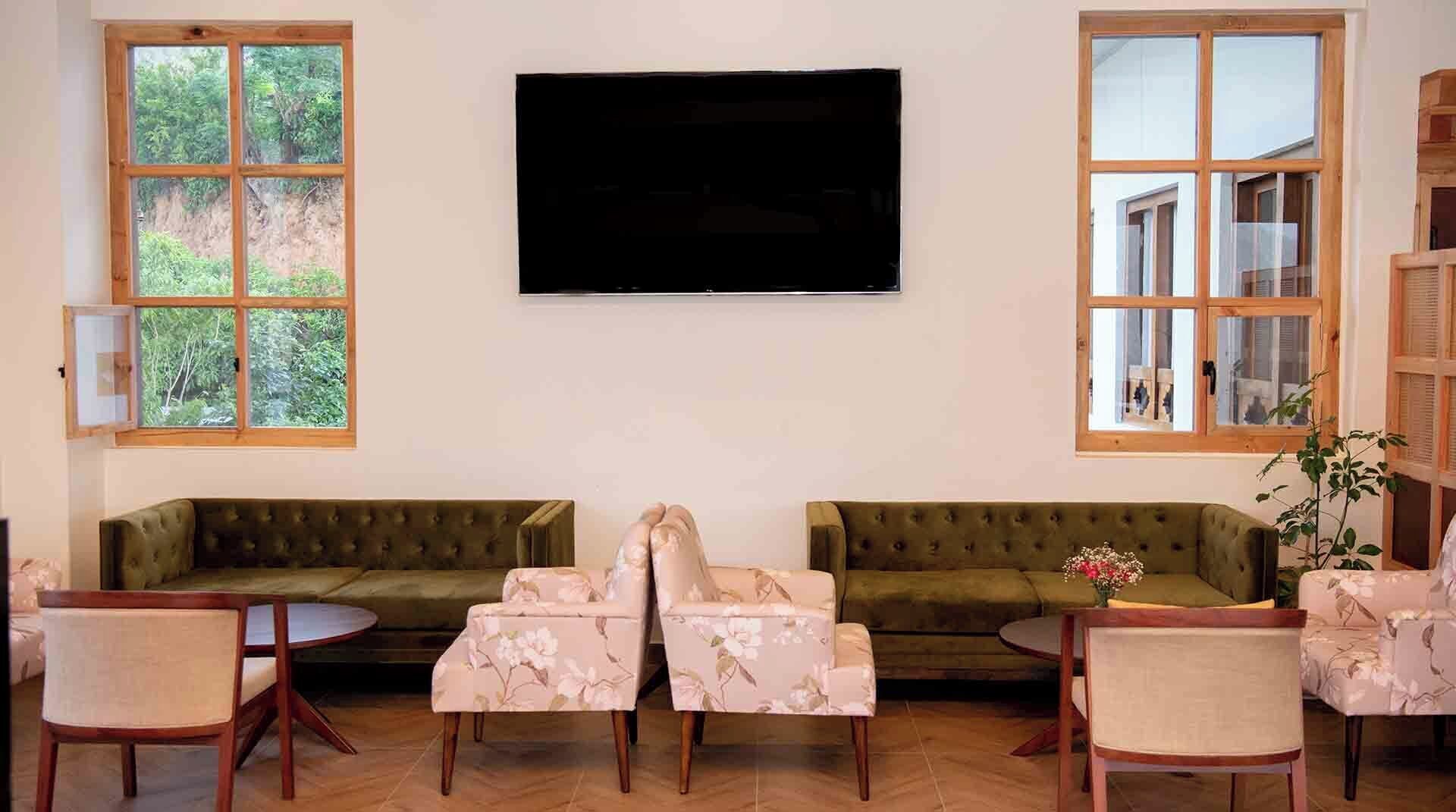 Uma sala de estar com dois sofás verdes, uma TV de tela plana e uma janela grande com vista para o verde.