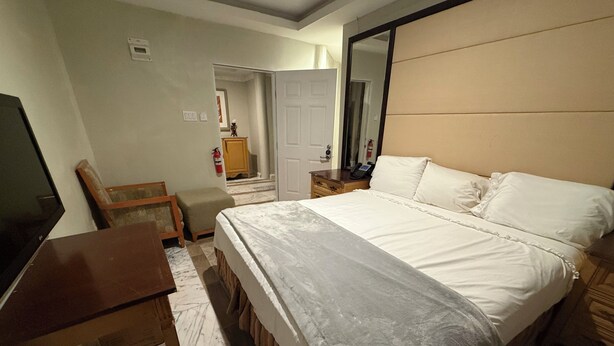 Quarto de hotel com cama, escrivaninha, cadeira, espelho e porta que dá para outro cômodo.