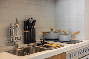 Cozinha com pia de aço inoxidável, torneira, bloco de facas e duas panelas sobre a bancada.