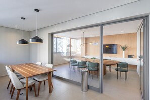 Uma sala de reuniões moderna com uma mesa de madeira, cadeiras cinzas e iluminação pendente.