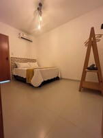 A bedroom with a bed, an air conditioning unit, a wooden ladder, and a door.
