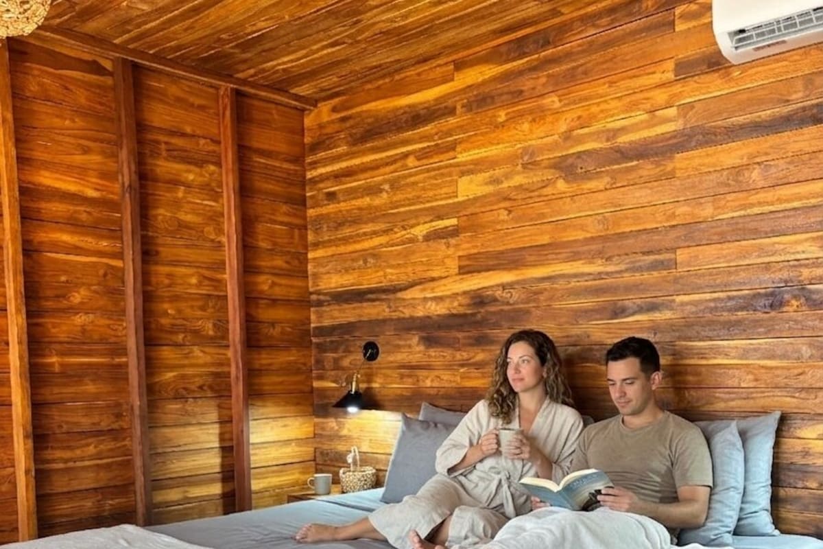 Quarto de madeira com uma cama, mesa de cabeceira e luminária.