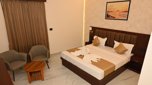 Quarto de hotel com uma cama grande, duas poltronas, uma pequena mesa de madeira e uma pintura de pôr do sol na parede.