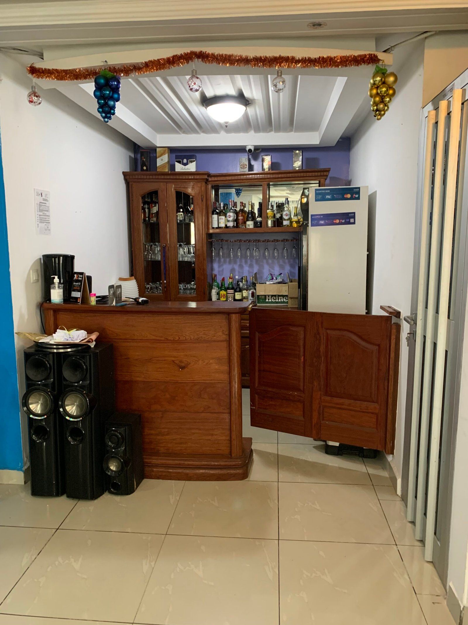 Uma área de bar com balcão de madeira, prateleiras com garrafas e geladeira.