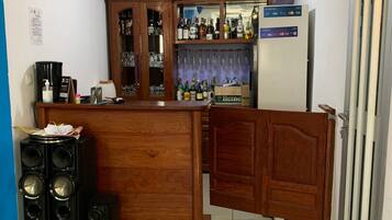 Uma área de bar com balcão de madeira, prateleiras com garrafas e geladeira.