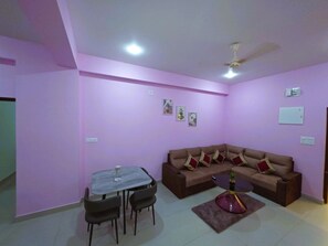 Uma sala de estar com um sofá marrom, uma mesa de jantar com cadeiras e um ventilador de teto.
