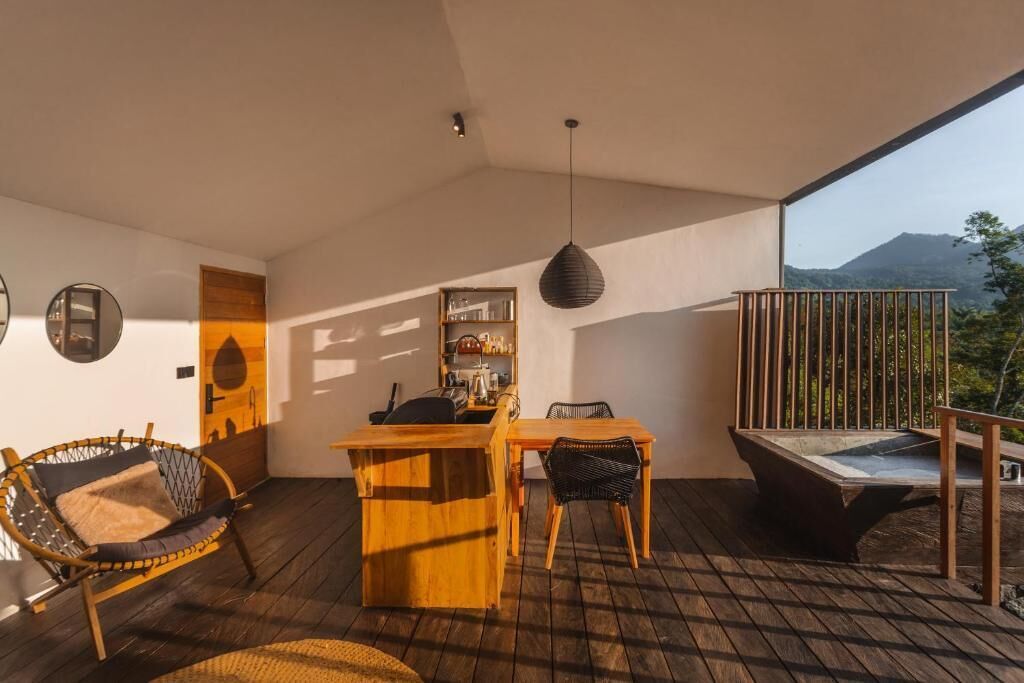 Um deck de madeira com área de refeições, luminária pendente e vista para uma montanha.
