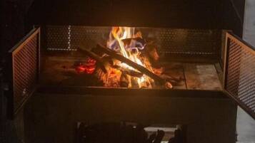Uma lareira de metal com fogo aceso no interior, rodeada por uma estrutura de tijolos.