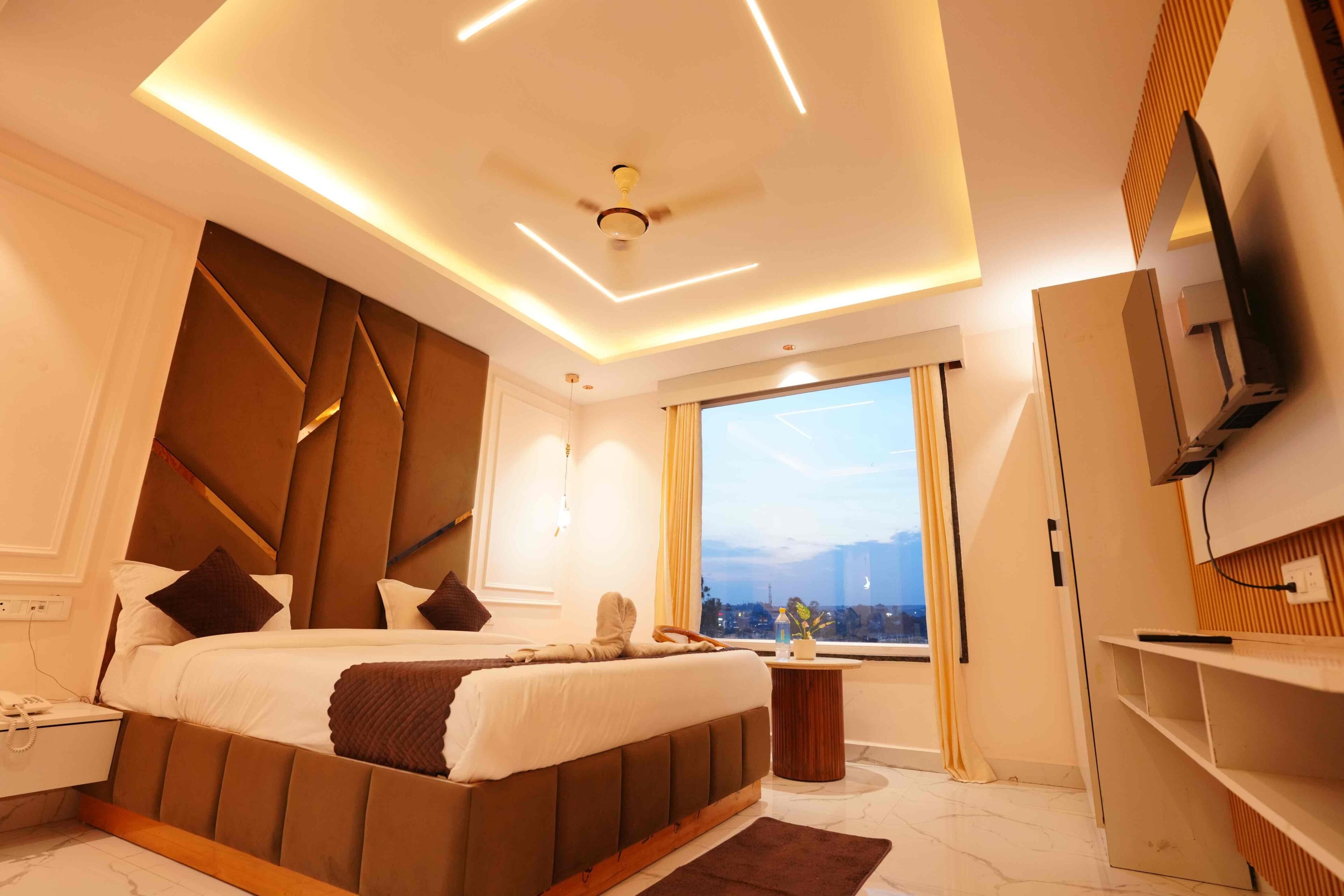 Quarto de hotel moderno com uma cama grande, televisão de tela plana, escrivaninha com telefone e janela com vista para a cidade.