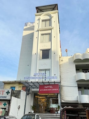 Hotel chamado 'Hotel Ayushman Ganga', com fachada moderna, entrada visível e placa de identificação.