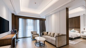 Quarto de hotel moderno com televisão de tela plana, sofá, mesa de centro, cama e escrivaninha.