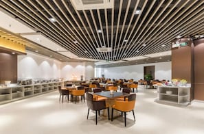 Uma ampla sala de jantar com várias mesas e cadeiras, um design de teto moderno e um ambiente limpo e bem iluminado.