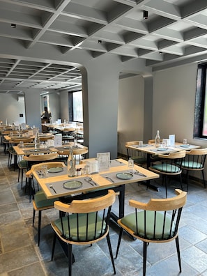 Restaurante com várias mesas e cadeiras, uma pessoa ao fundo e design moderno no teto.