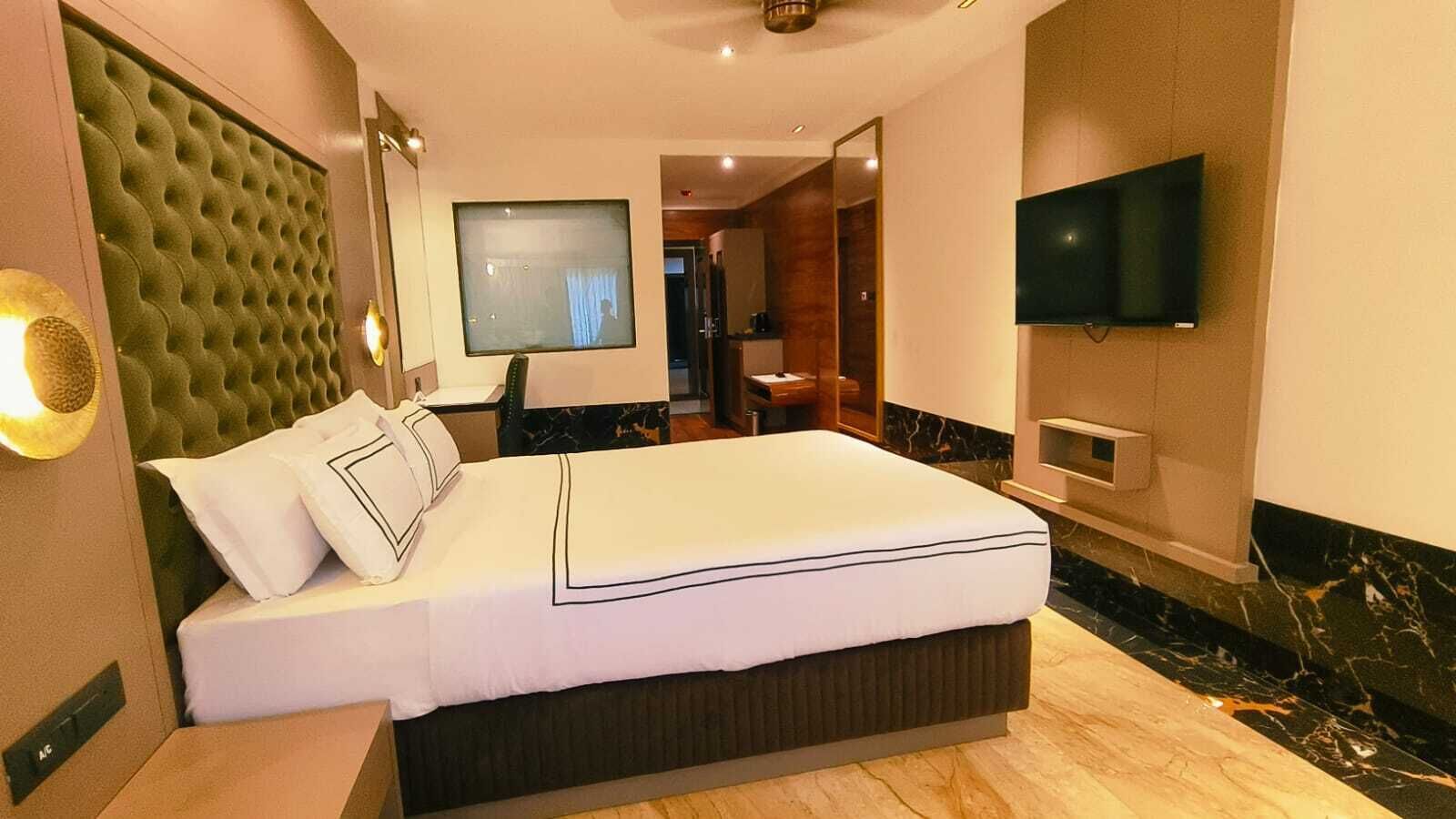 Quarto de hotel com uma cama grande, televisão, espelho e piso de mármore.