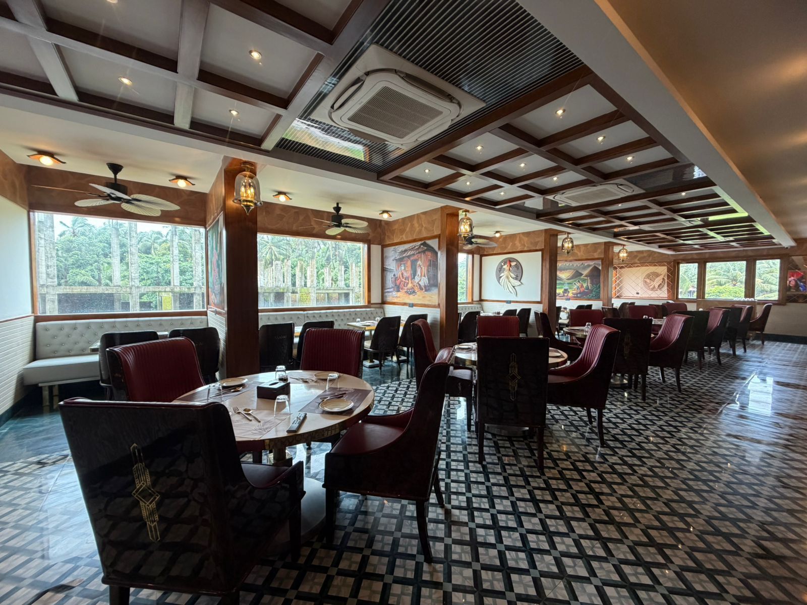 Um restaurante com várias mesas e cadeiras, grandes janelas com luz natural e um chão estampado.