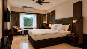 Quarto de hotel com cama grande, escrivaninha, cadeira, toucador com espelho e janela com cortinas.