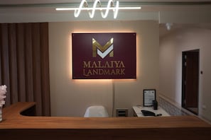 Uma mesa de recepção com uma placa indicando 'MALAIYA LANDMARK' e um lustre moderno acima.
