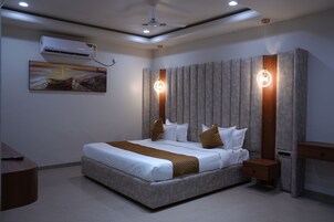 Quarto de hotel moderno com uma cama grande, cabeceira com iluminação embutida, um quadro na parede e um aparelho de ar condicionado.
