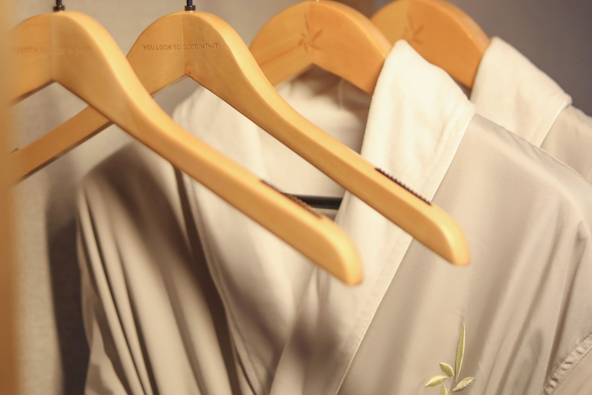 Suporte de madeira para cabides com três cabides, cada um segurando uma peça de roupa branca.