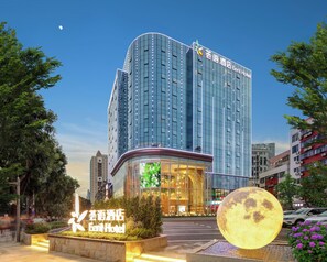 Hotel com fachada de vidro moderna, uma placa bem visível e uma grande escultura iluminada de lua.