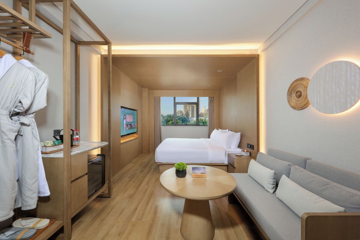 Quarto de hotel com cama, sofá, escrivaninha e roupão pendurado em um suporte.