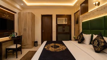 Quarto de hotel com cama, escrivaninha, cadeira, guarda-roupa e televisão.