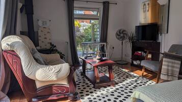 Uma sala de estar com uma poltrona de couro, uma mesa de centro de madeira, um tapete estampado, uma televisão e uma janela com cortinas.