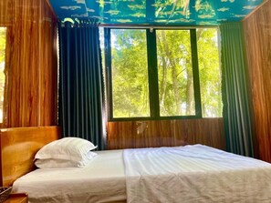 Quarto com cama, cortinas e vista para as árvores pela janela.