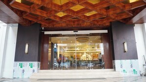 Entrada de um edifício com estrutura de teto em madeira e portas de vidro.
