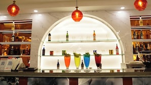 Uma área de bar com bancada de mármore, prateleiras com garrafas e bebidas coloridas.
