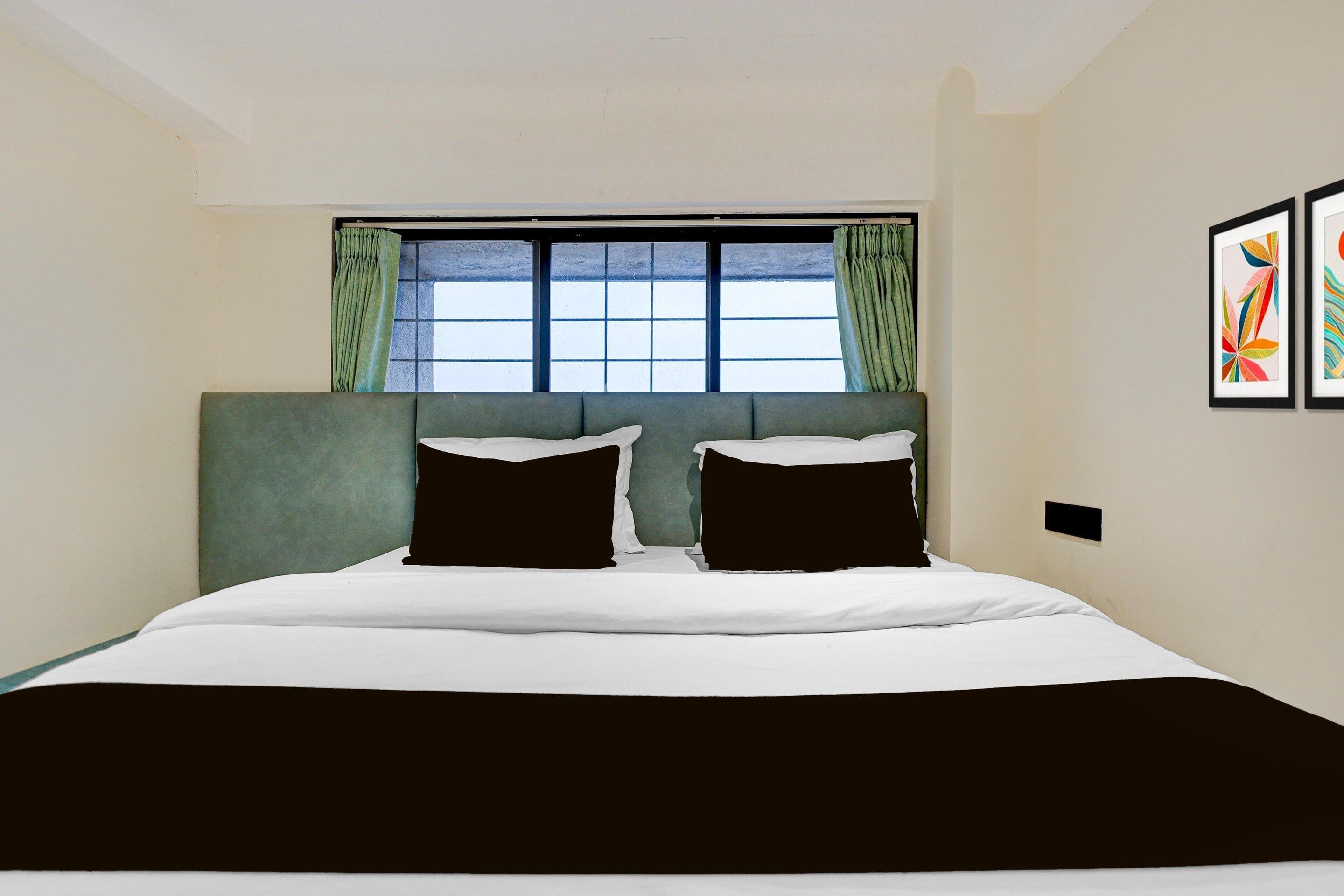 Quarto de hotel com cama, janela com cortinas e duas fotos emolduradas na parede.
