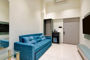 Uma sala de estar moderna com um sofá azul, uma mesa de centro de vidro, uma TV de tela plana e uma porta.