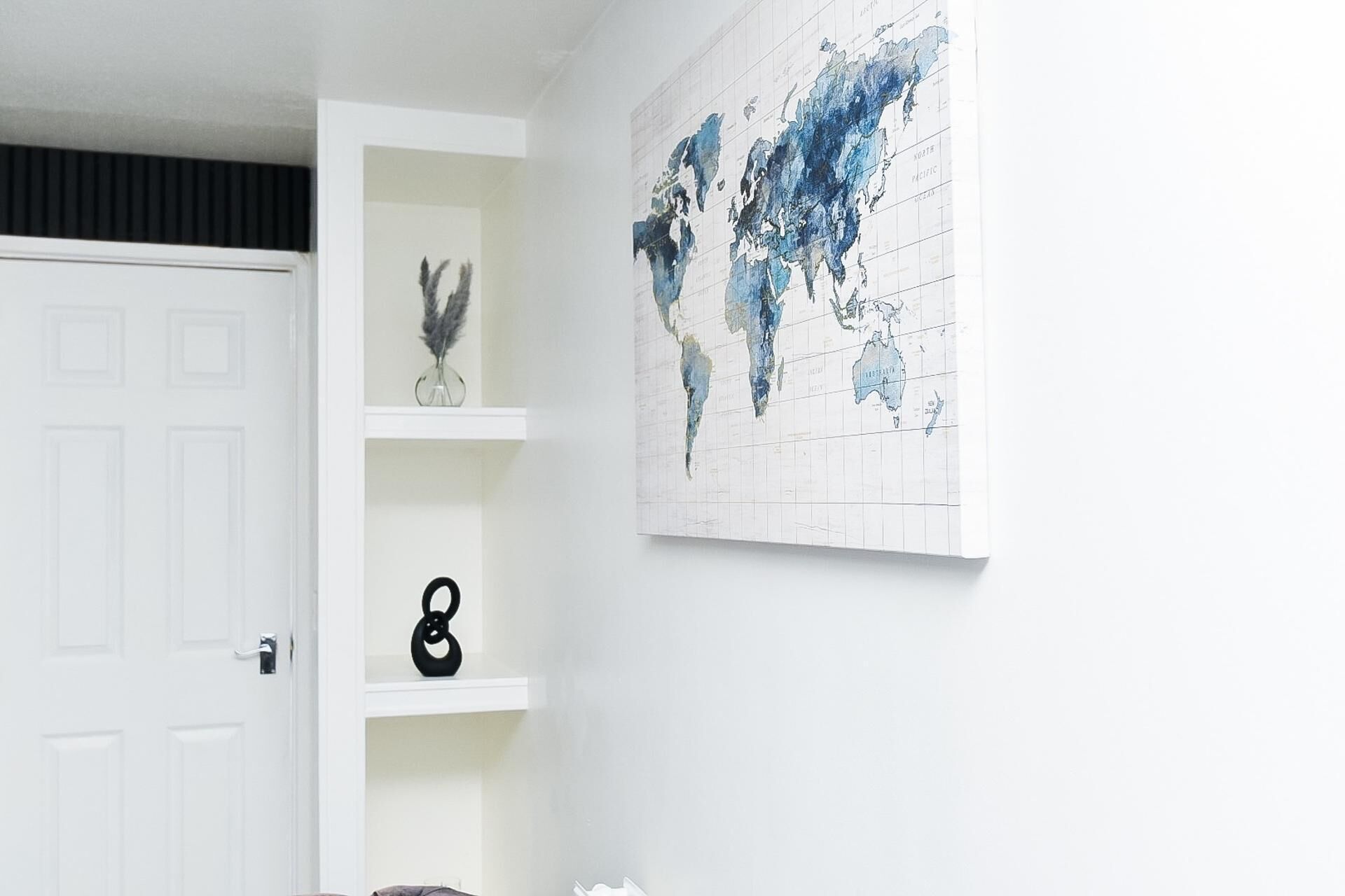 Quarto com porta branca, um mapa-múndi na parede e uma estante com objetos decorativos.