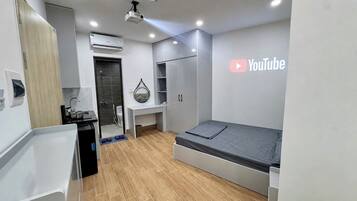 Quarto compacto com cama, escrivaninha, espelho e o logotipo do YouTube na parede.