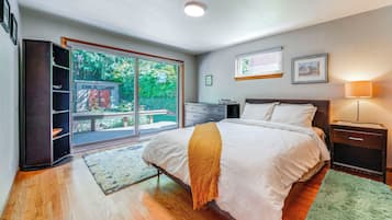 Quarto com cama, mesa de cabeceira, cômoda, janela com vista para o verde e luminária no teto.