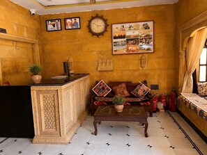 Um quarto com uma mesa de recepção, um sofá com almofadas estampadas, um relógio de parede e uma colagem emoldurada de imagens.