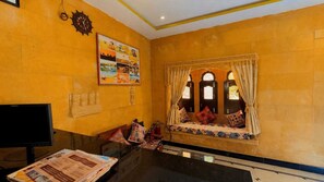 Um quarto com uma janela grande, uma cama com almofadas, uma televisão de tela plana e um relógio de parede.