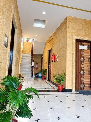 Um saguão de hotel com piso de mármore, escada, plantas em vasos e porta de madeira com design decorativo.