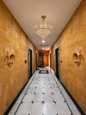Um corredor com um candelabro, paredes estampadas e chão ladrilhado.